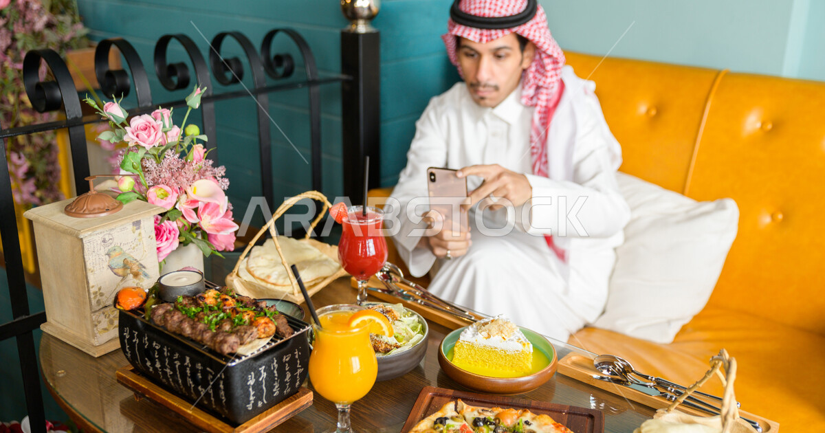 A Saudi Arabian Gulf man sitting at the dining table and using a mobile ...