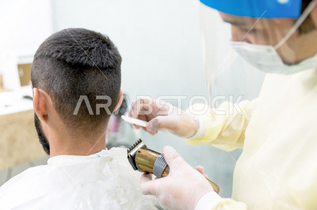 A Saudi Arabian Gulf man visits a barber shop. The barber uses the ...