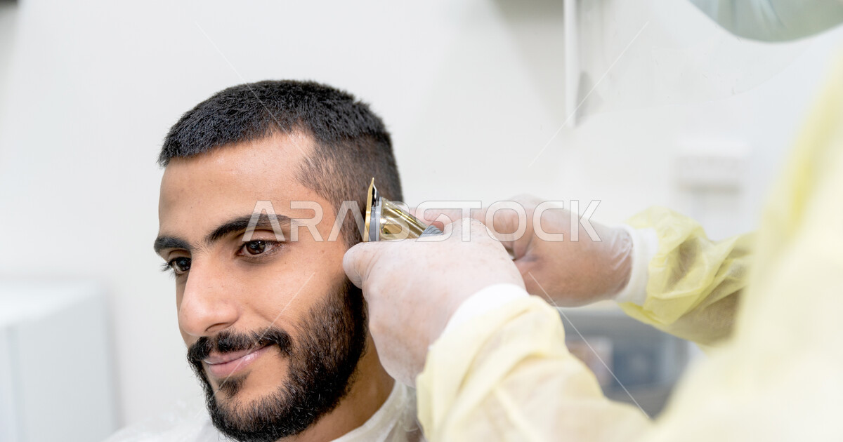 A Saudi Arabian Gulf man visits a barber shop. The barber uses the ...