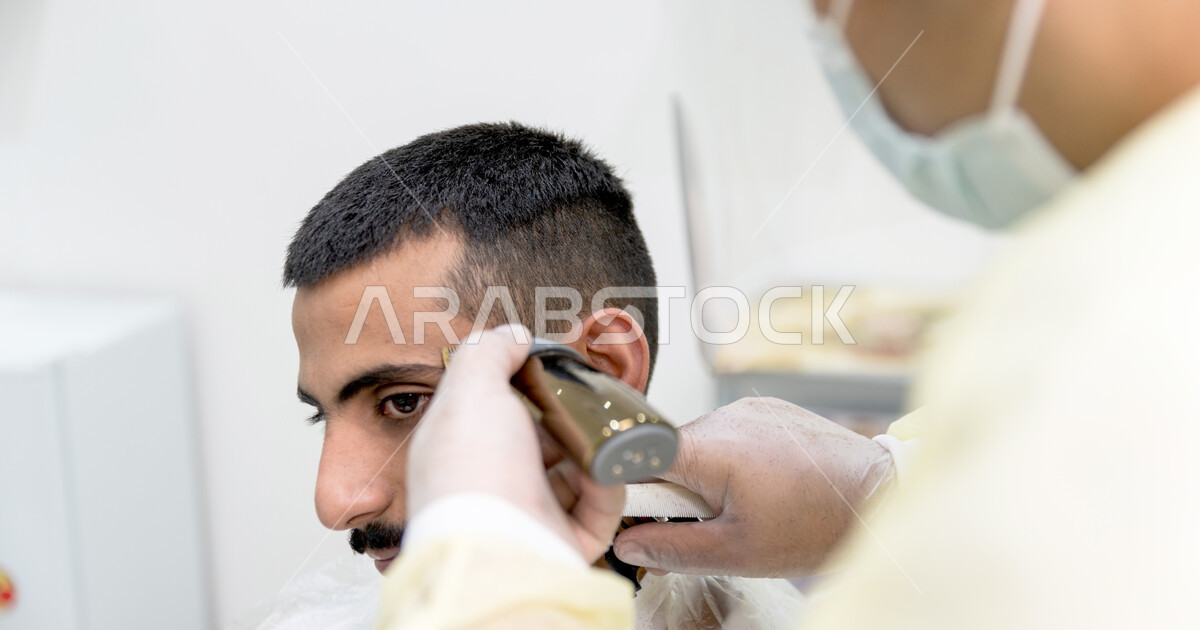 A Saudi Arabian Gulf man visits a barber shop. The barber uses the ...