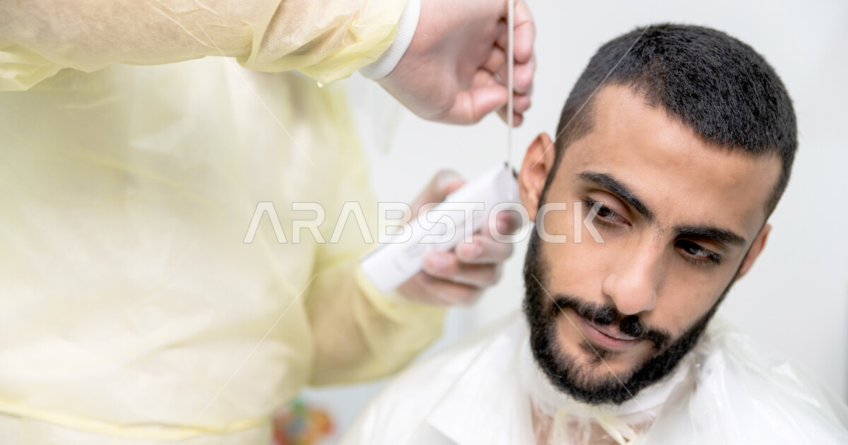 A Saudi Arabian Gulf man visits a barber shop. The barber uses the ...