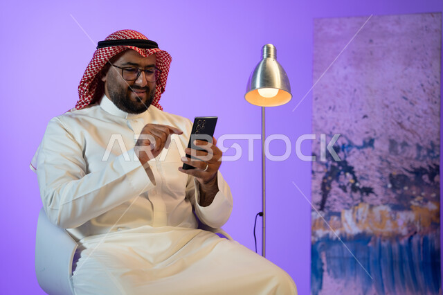 Sending a text message via mobile phone, a smiling Saudi Gulf Arab man ...