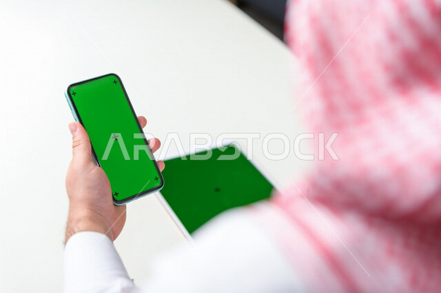 A Saudi Gulf businessman uses his mobile phone with a green background ...