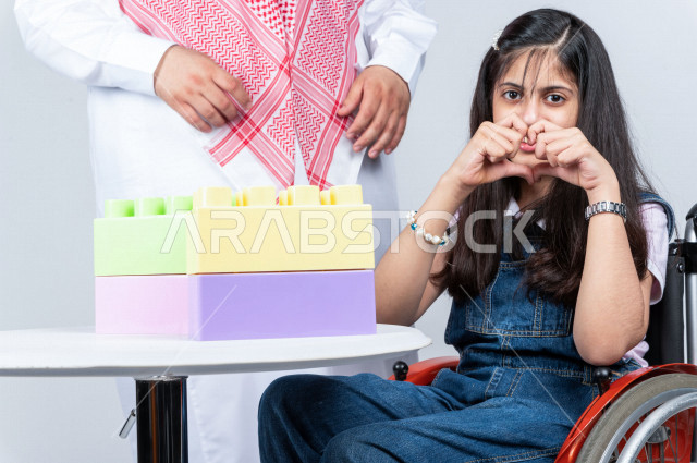 Portrait of a Saudi Gulf girl in a wheelchair with her father, spending ...