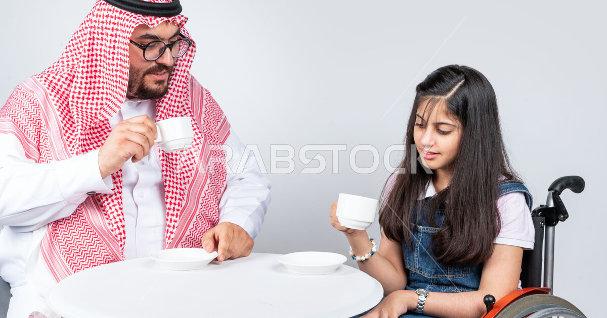 Portrait of a Saudi Arabian Gulf child in a wheelchair with her father ...
