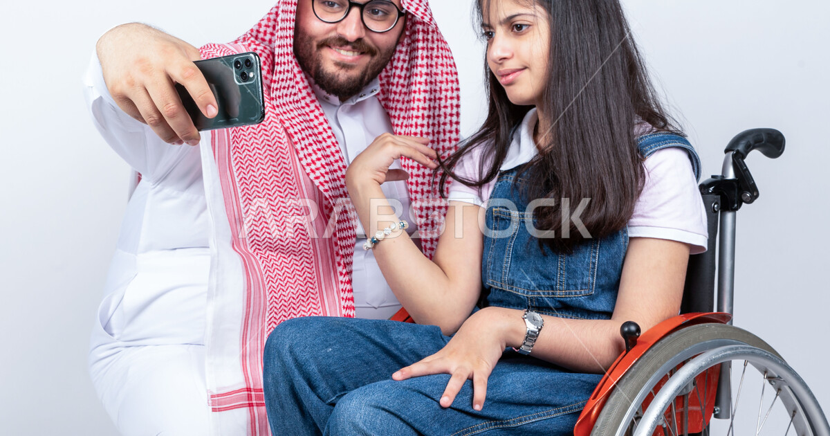 Portrait of a Saudi Arabian Gulf child in a wheelchair with her father ...