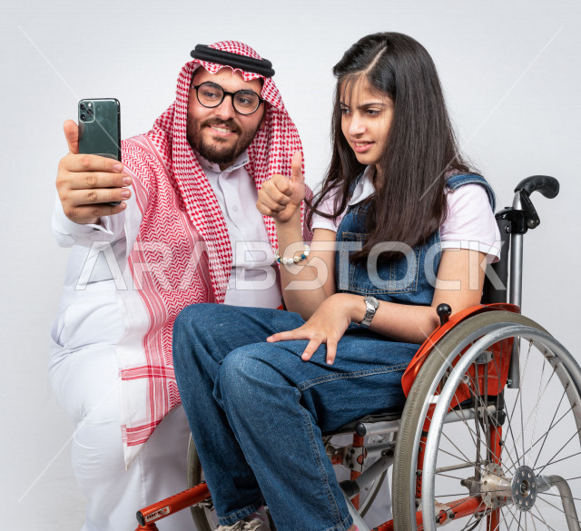 Portrait of a Saudi Arabian Gulf child in a wheelchair with her father ...