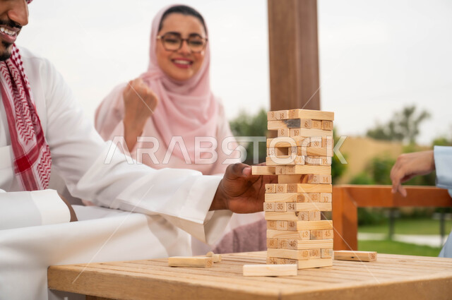 A Saudi Gulf Arab family plays Jenga outdoors, stacking pieces and ...
