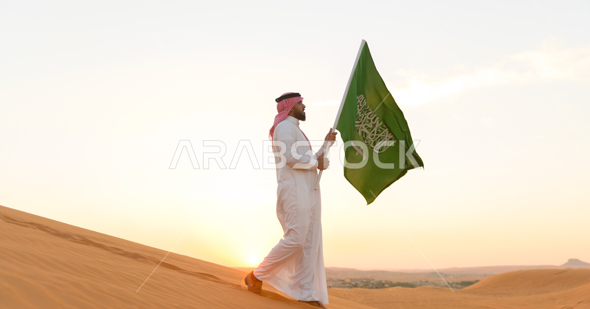 A Saudi man carries the Saudi flag over the hills of one of the desert ...