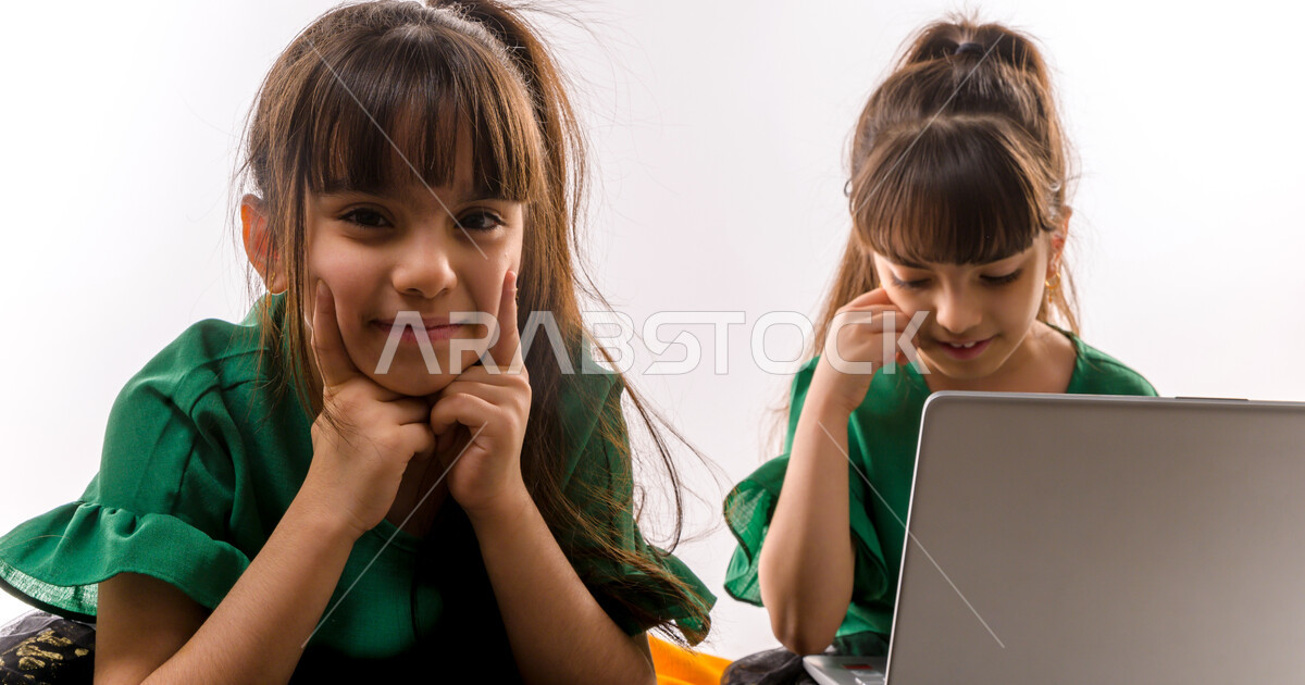 Portrait of two Saudi twin sisters using a laptop, studying remotely ...