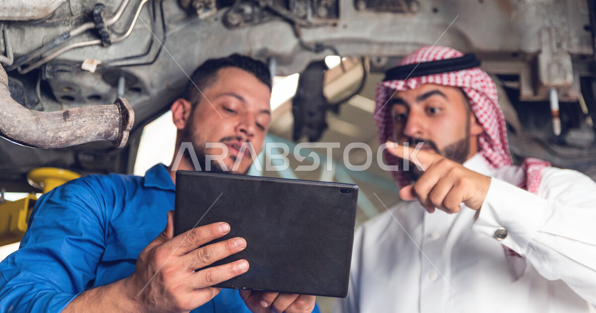A Saudi Arabian man inside the car workshop, uses the tablet device to ...