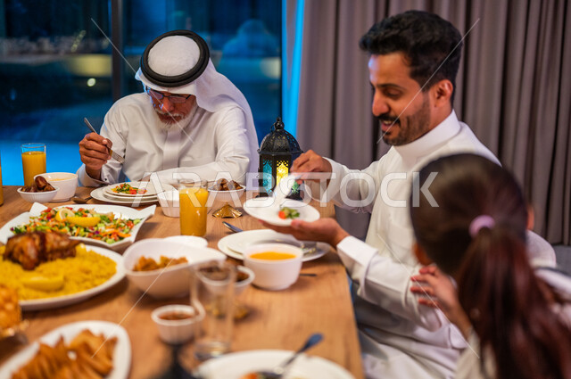 A Saudi Gulf Arab man pours food for his daughter, serves juices and ...