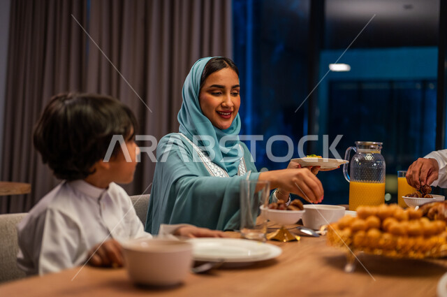 A Saudi Gulf Arab mother pouring food for her child, serving juices and ...