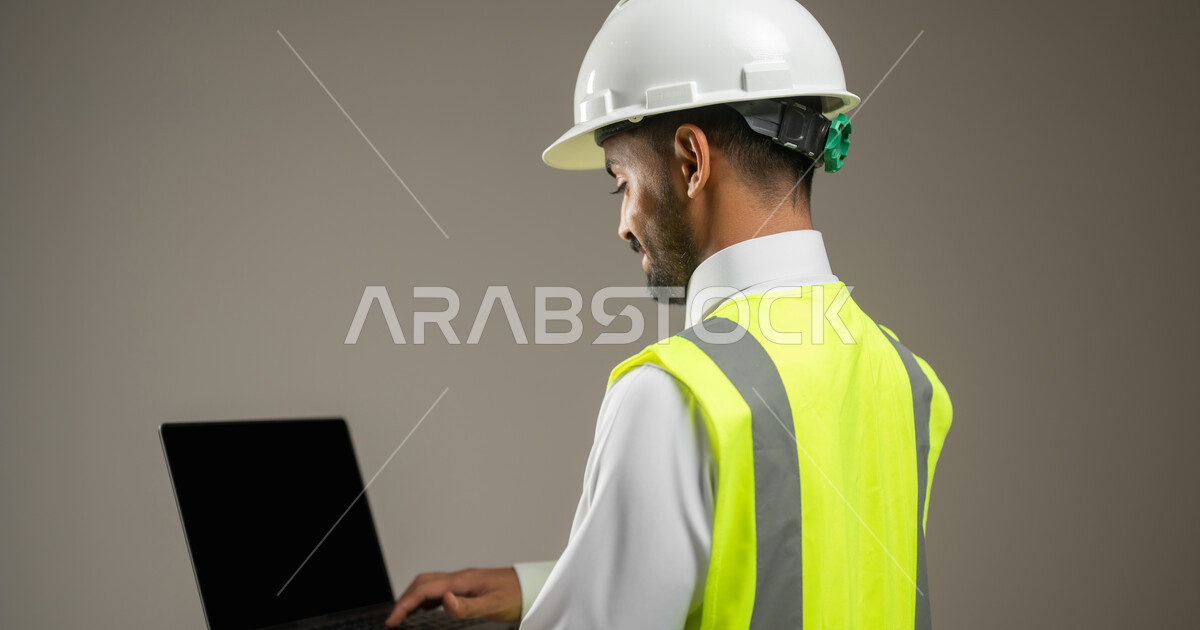 A close-up portrait of a Saudi Gulf Arab engineer holding a laptop, a ...