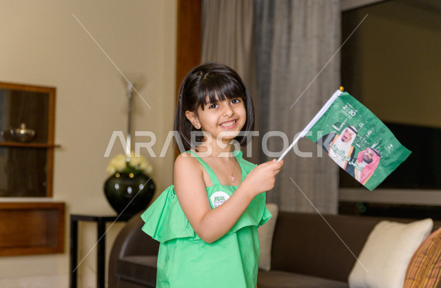 A Saudi girl wears a green dress and holds the Saudi flag to celebrate ...