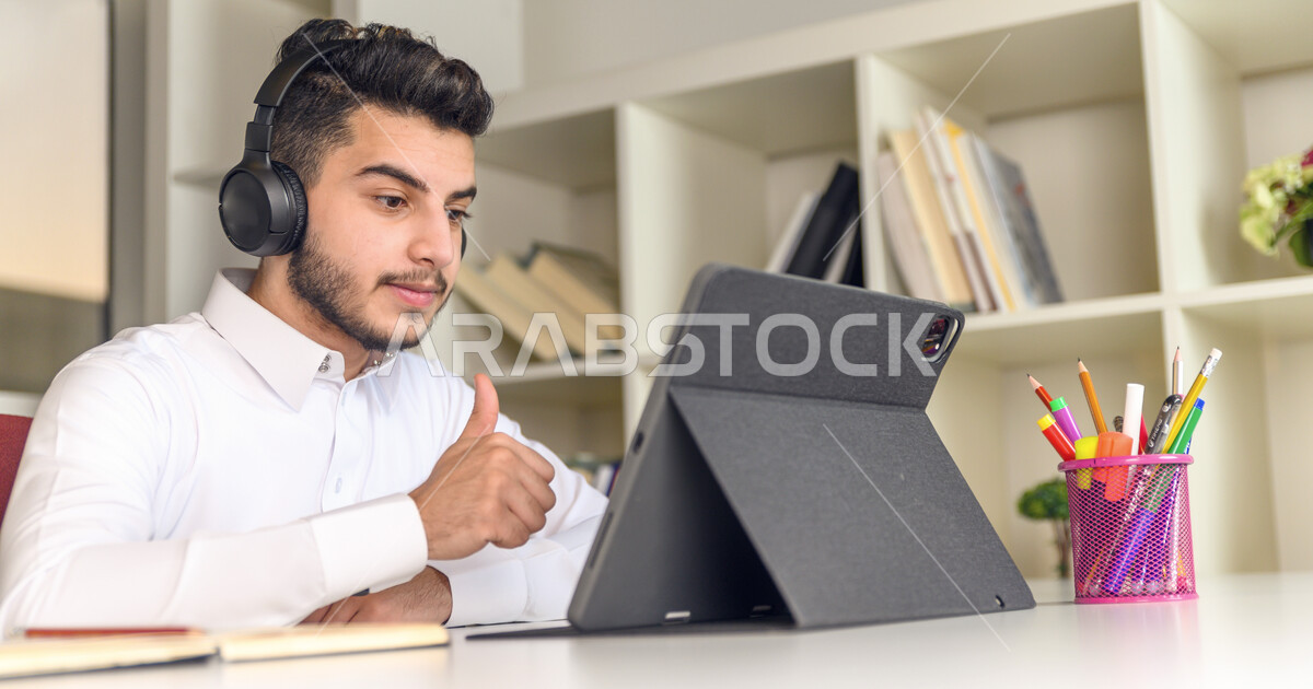 A young Saudi Arabian Gulf man studies at home using a tablet device ...