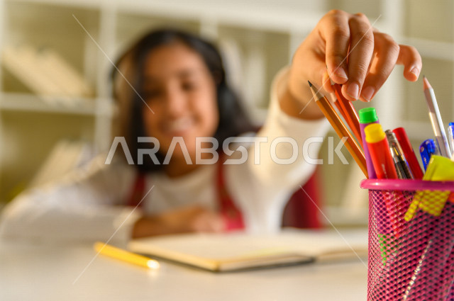 A happy Saudi Gulf student studying at home, choosing a suitable pen to ...