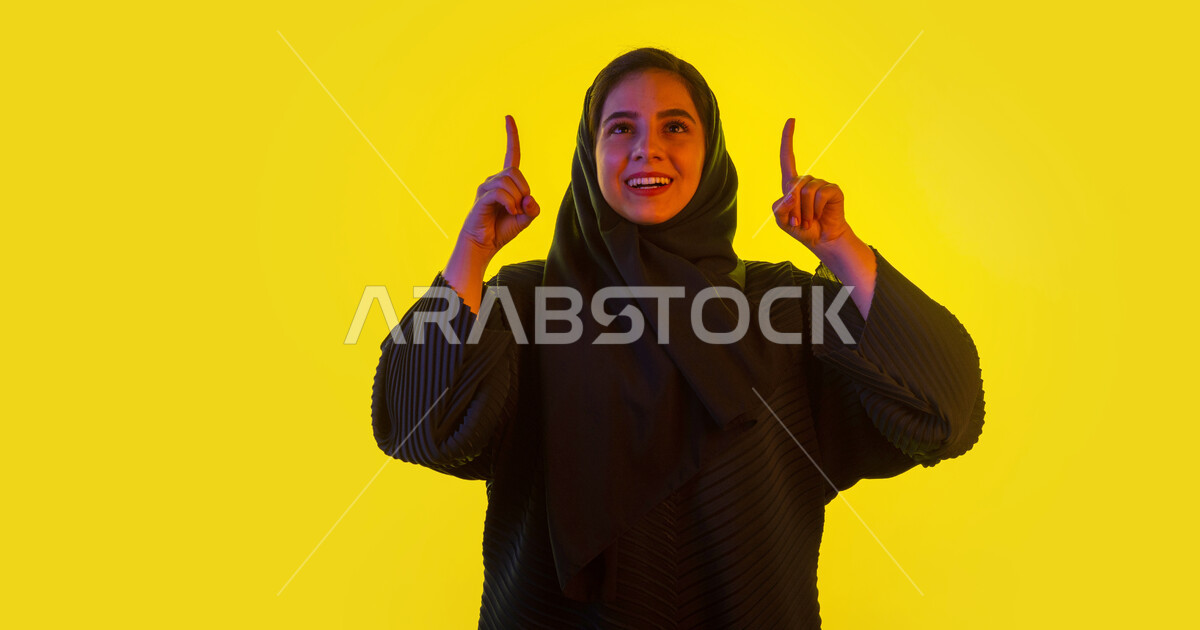 Portrait of a happy Saudi Arabian Gulf woman, pointing her finger up ...