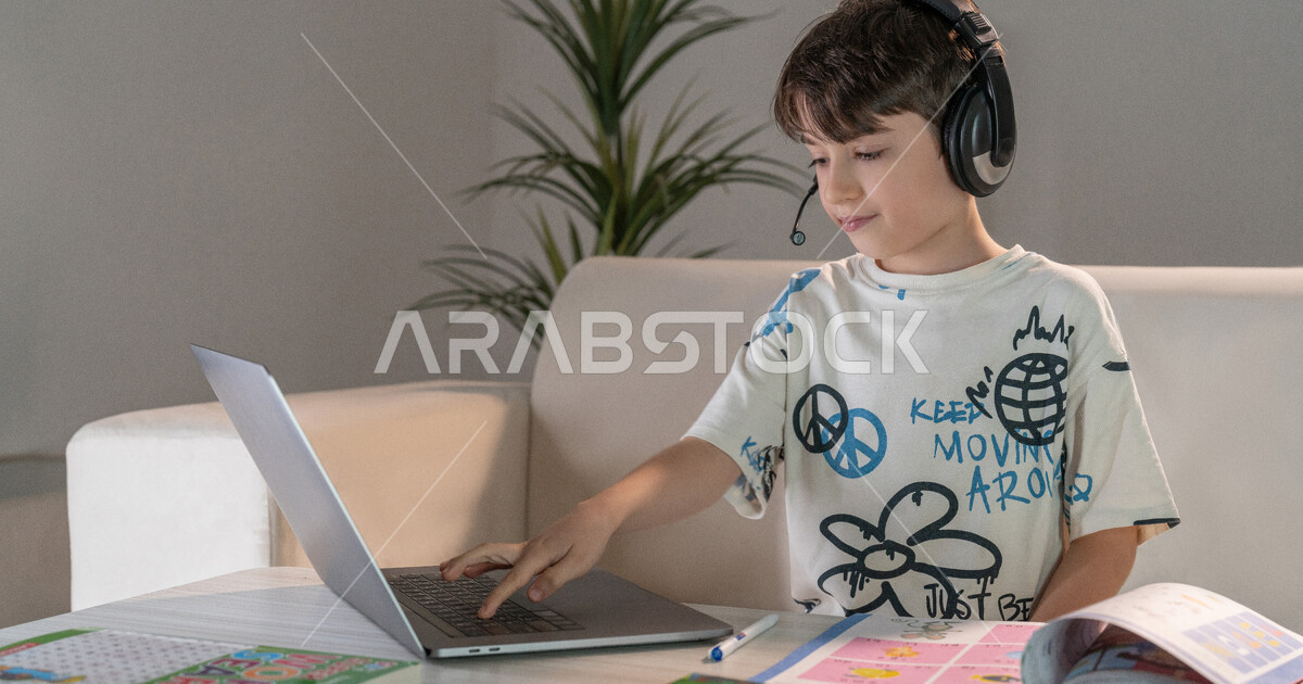 متابعة الحصص الدراسية عبر الاونلاين، ولد عربي خليجي إماراتي يستخدم الحاسب المحمول لحل الواجبات ...