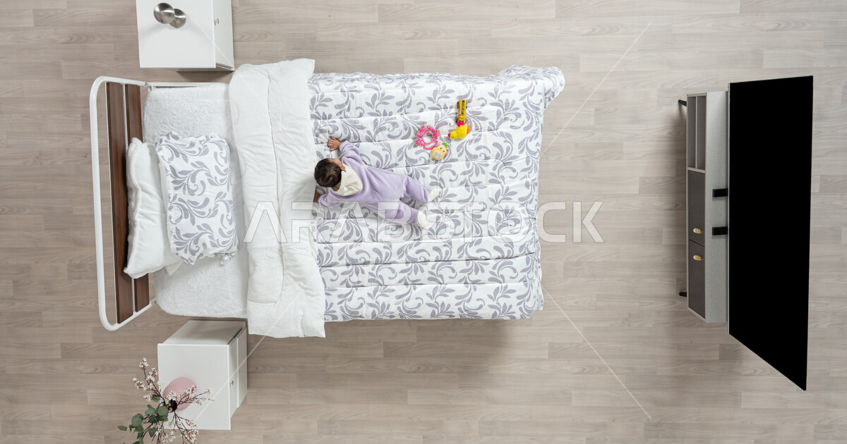 العنايه والرعايه بالاطفال، بورتريه عامودي علوي لطفل عربي سعودي خليجي مستلق على بطنه يحبو بلطف ...