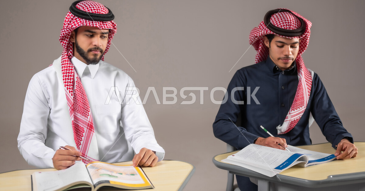 End-of-semester exams, portrait of two Gulf Arab students wearing traditional thobes and shemagh ...