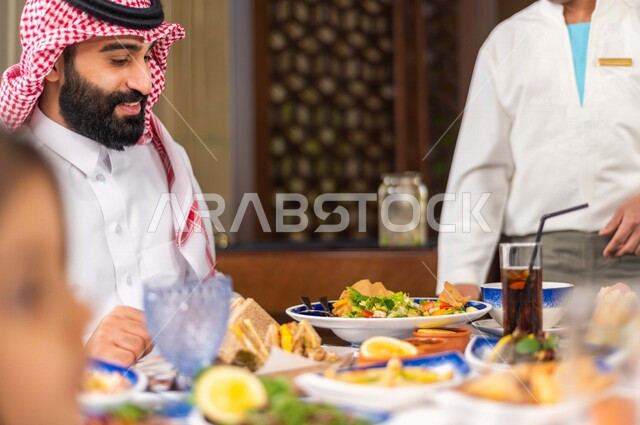 A Saudi Arabian Gulf family sitting in the restaurant, the waiter ...