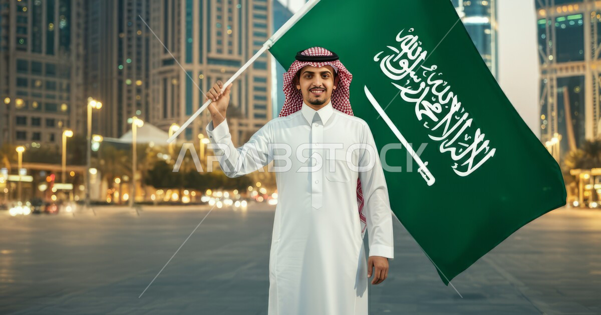 A Saudi Gulf man holding the flag of the Kingdom of Saudi Arabia in his ...