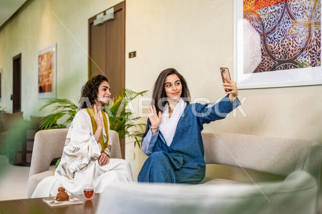 Two Saudi Arabian Gulf girls sitting together happily taking a selfie ...