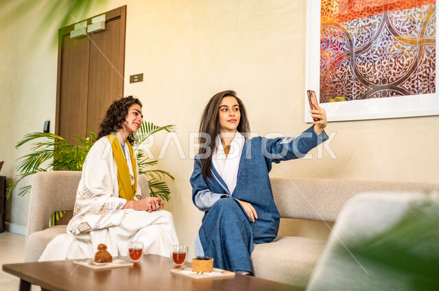 Two Saudi Arabian Gulf girls sitting together happily taking a selfie ...