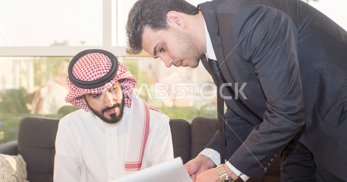 A Saudi Arabian Gulf businessman holding papers in his hand, discussing ...