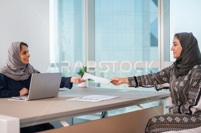 A Saudi Arabian Gulf employee gives her colleague a paper on the ...