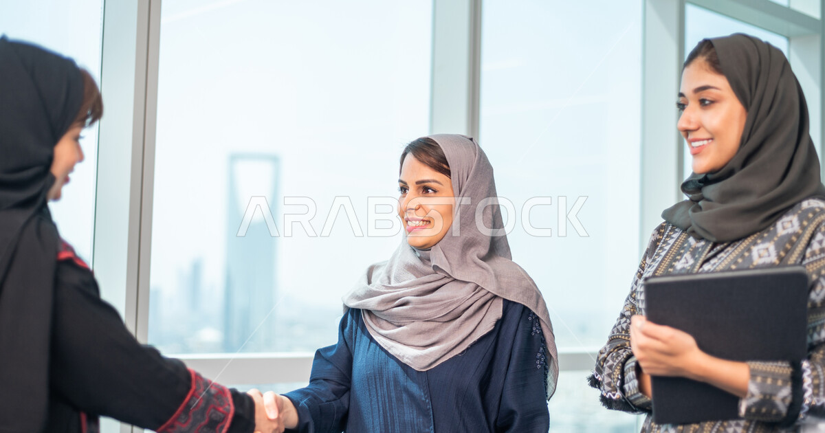 Two Gulf Arab women shaking hands inside the company, a work agreement ...