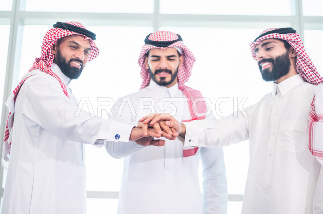 A picture of a Saudi Gulf work team putting their hands on top of each ...