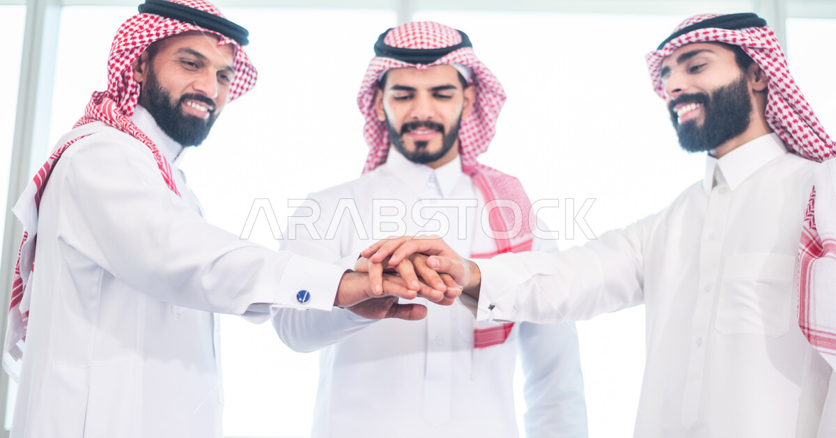 A picture of a Saudi Gulf work team putting their hands on top of each ...