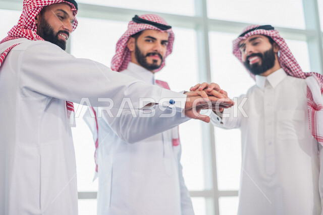 A picture of a Saudi Gulf work team putting their hands on top of each ...