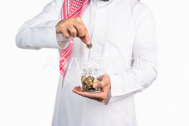 Portrait of a Gulf Arab man, saving and saving money in a glass bowl ...