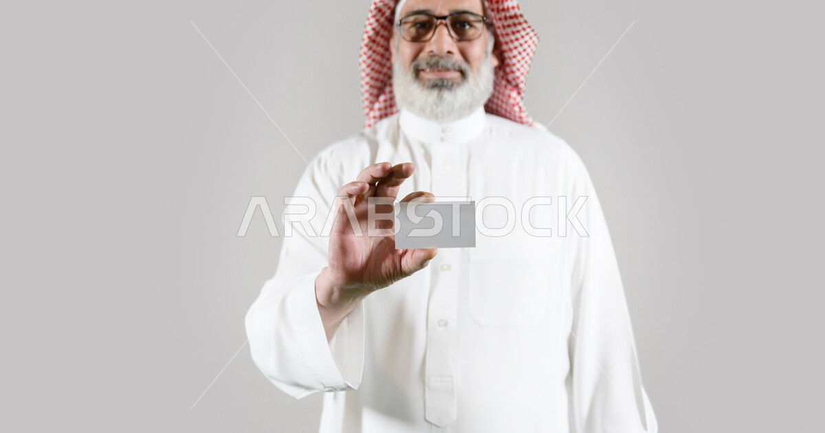 Portrait of a saudi old man holds a personal card in white Thobe dress ...