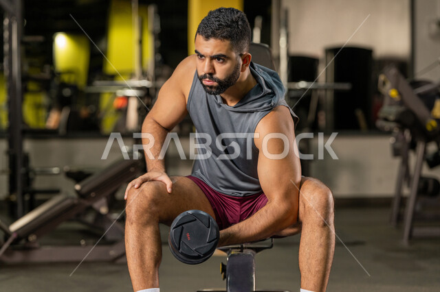 Bodybuilding, using weights, a young Arab Gulf Emirati man wearing ...
