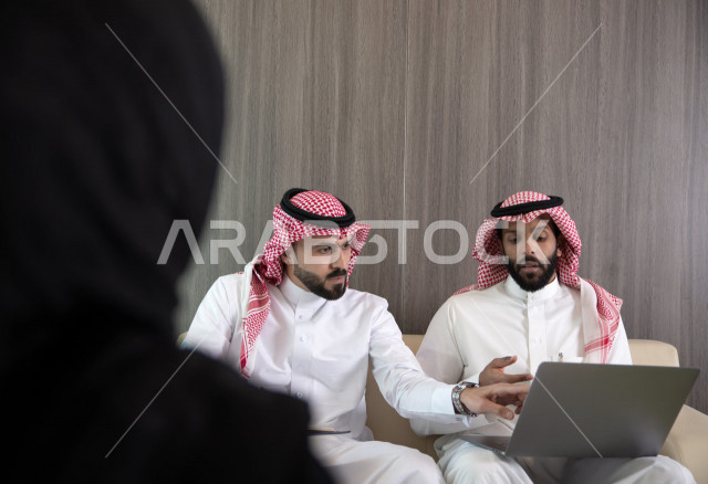 A Saudi Arabian Gulf work team, a businessman using a laptop computer ...