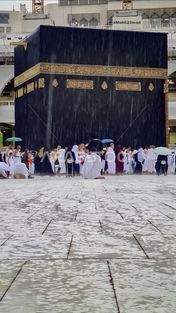 A group of pilgrims wearing ihram clothes and masks circumambulate the ...