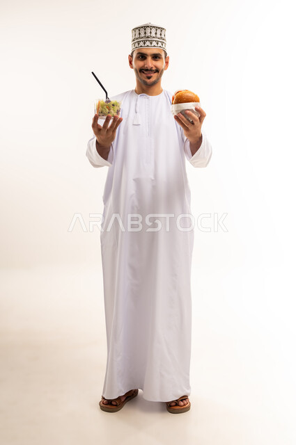 Eating fast food, portrait of smiling Omani Gulf Arab man wearing ...