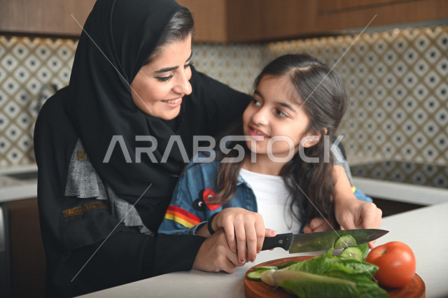 A Saudi Arabian Gulf woman helps her daughter chop vegetables, prepare ...