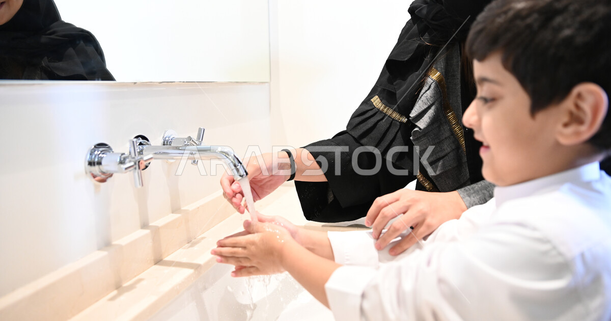 A Saudi Arabian Gulf woman helps her son wash his hands, clean hands ...