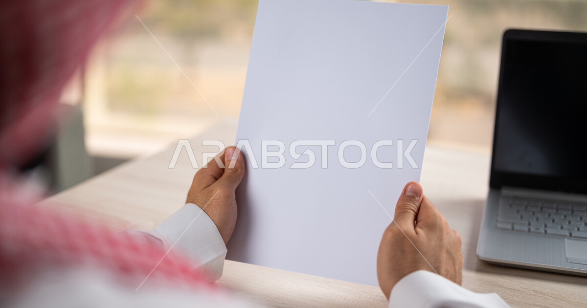 Close-up of the hand of a Saudi Arabian Gulf man holding work papers ...