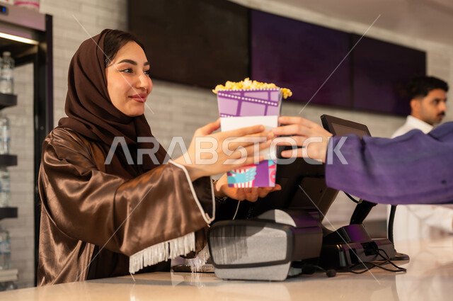 Enjoying popcorn, a smiling Saudi Arabian Gulf woman wearing an abaya ...