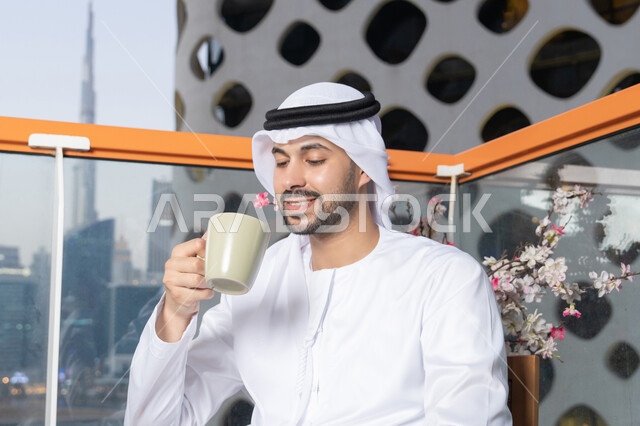 Enjoying hot drinks, an Emirati Gulf Arab man wearing a white kandura ...