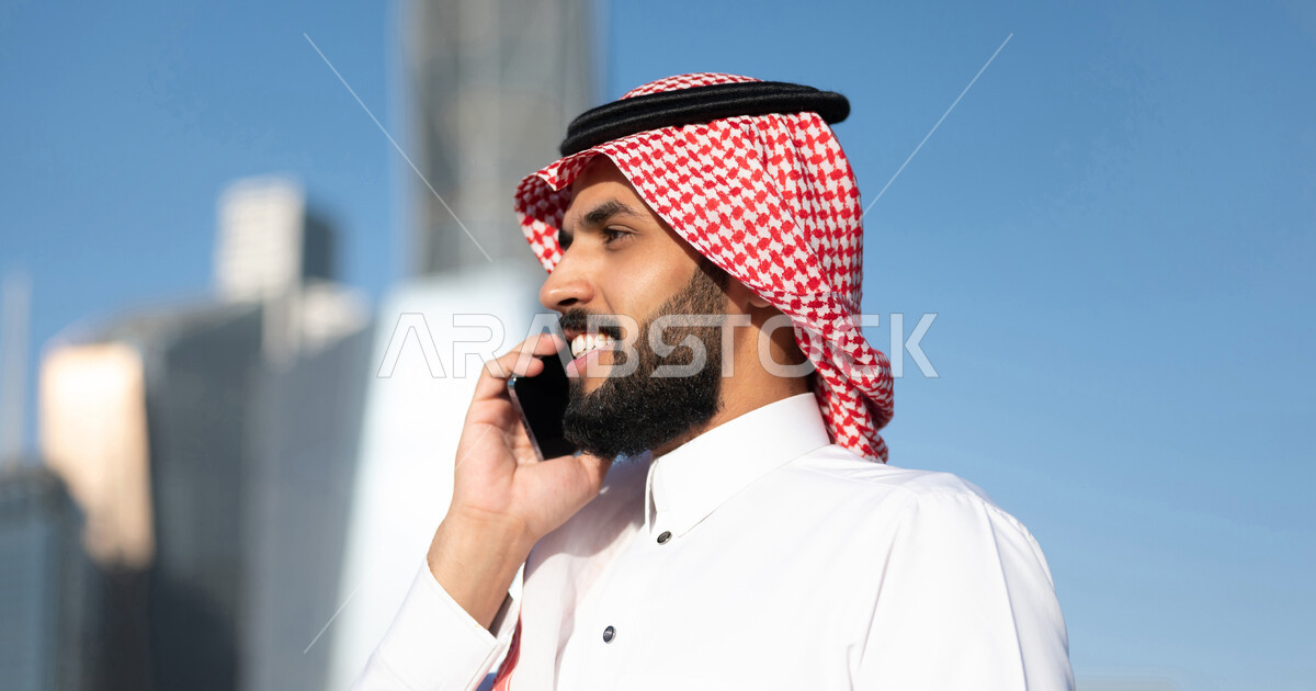 A smiling Saudi Arabian Gulf Arab man with a mobile phone making a ...