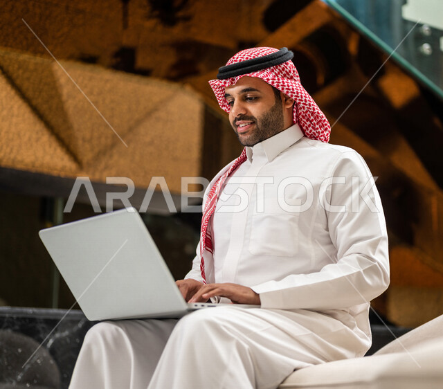 A Saudi Gulf man inside a tourist hotel, using a laptop computer to ...