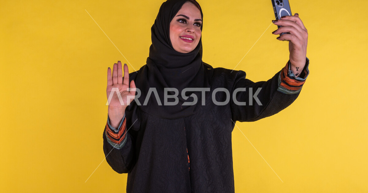 Portrait of a smiling Saudi Arabian Gulf woman using a mobile phone to ...