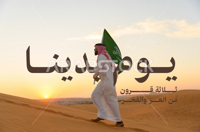 A Saudi Arabian Gulf man carrying the Saudi flag, walking in the desert ...